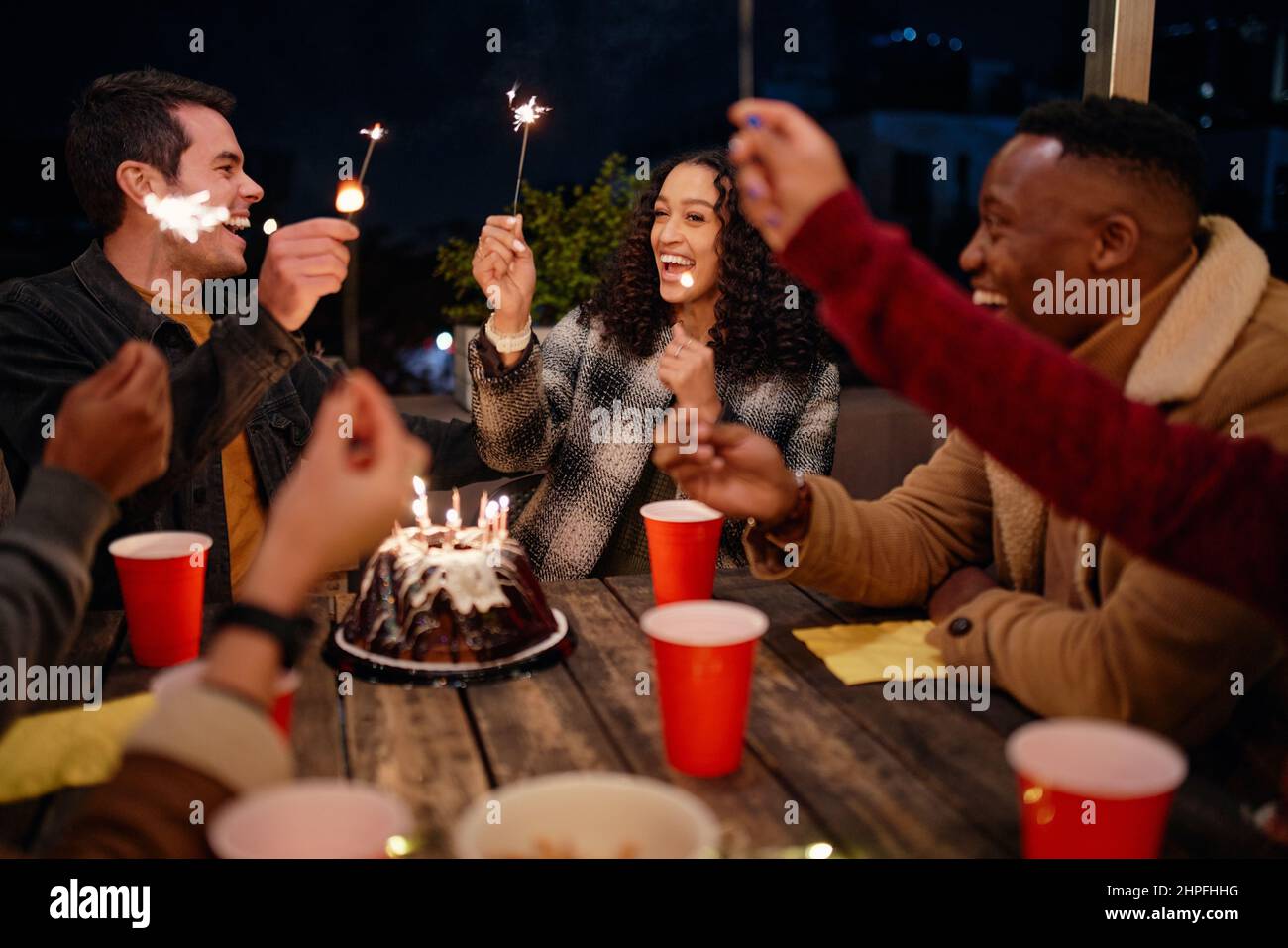 Group of diverse young adults sitting at singing happy birthday at ...