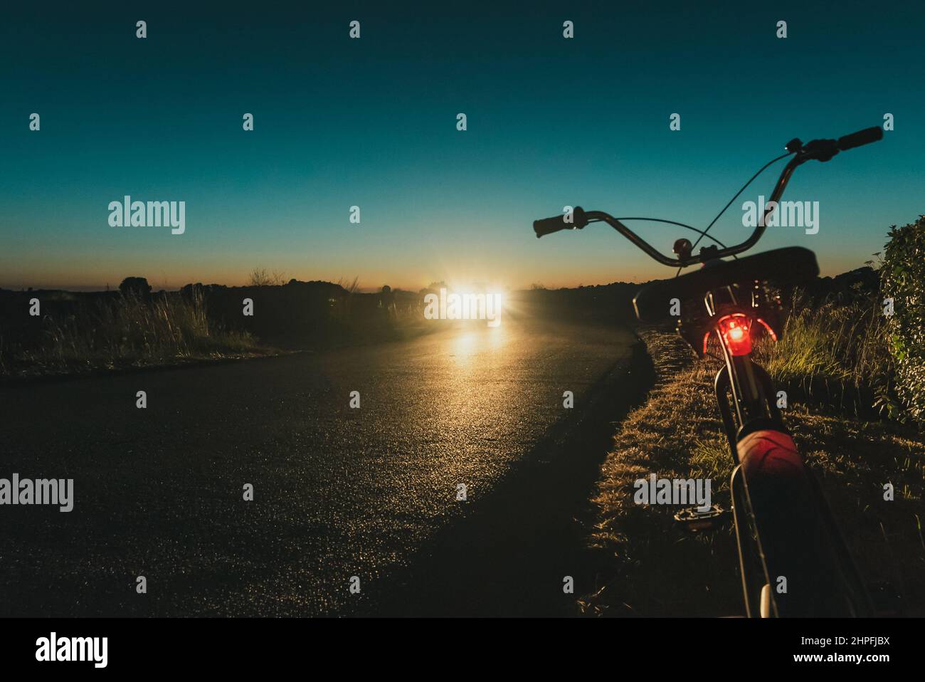 Bike on the low side of the road with red light on crossing car head ...