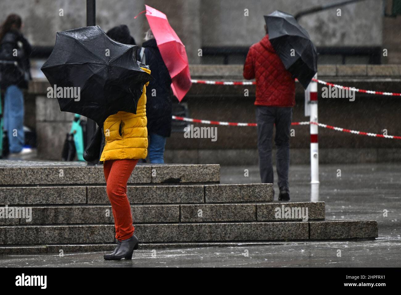 Cologne, Germany. 21st Feb, 2022. Passers-by struggle with the wind and ...