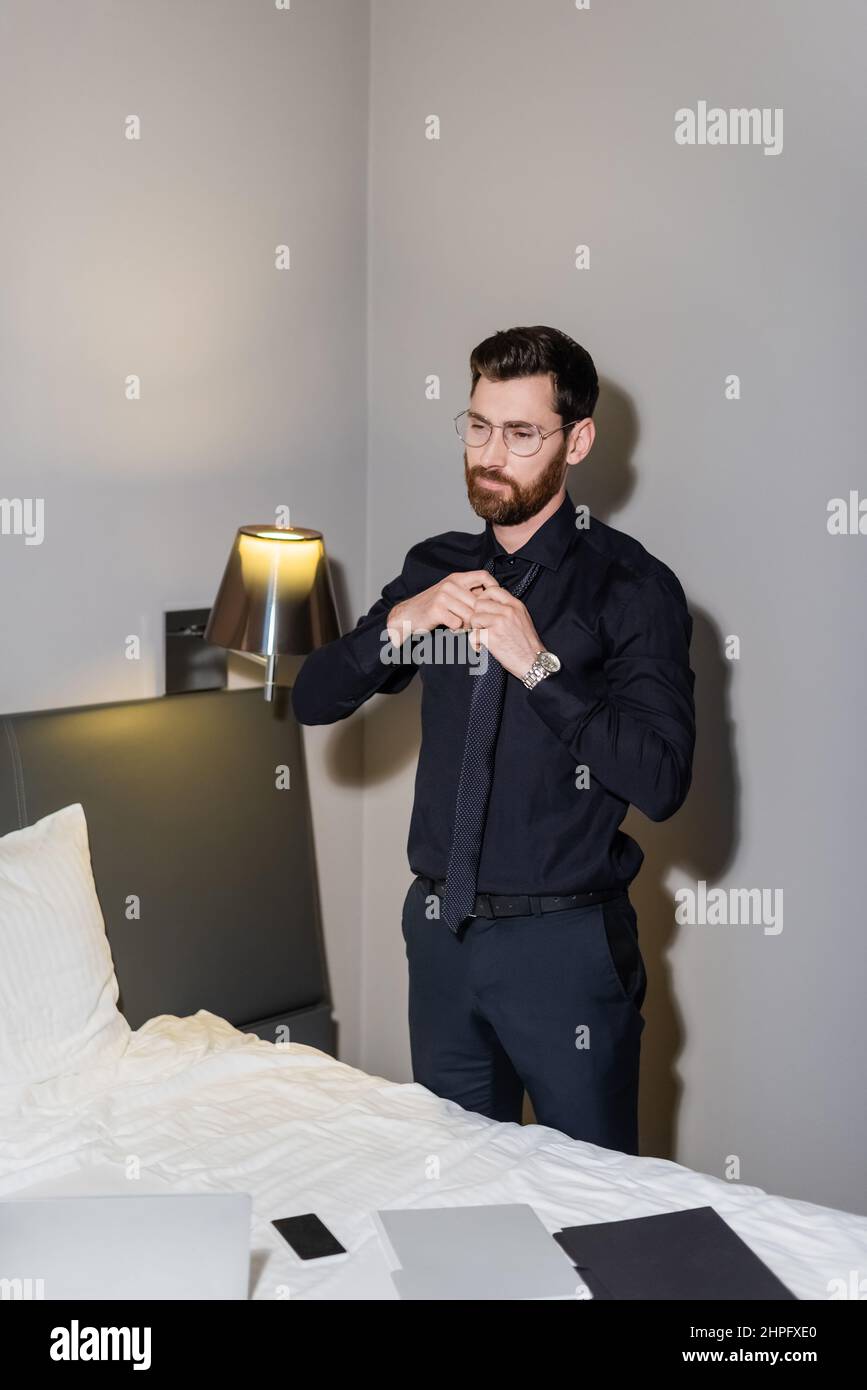 bearded man in eyeglasses adjusting tie in hotel Stock Photo - Alamy