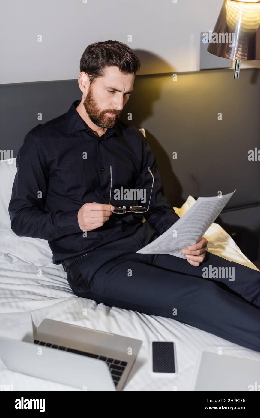 bearded man holding eyeglasses and looking at document in hotel Stock ...