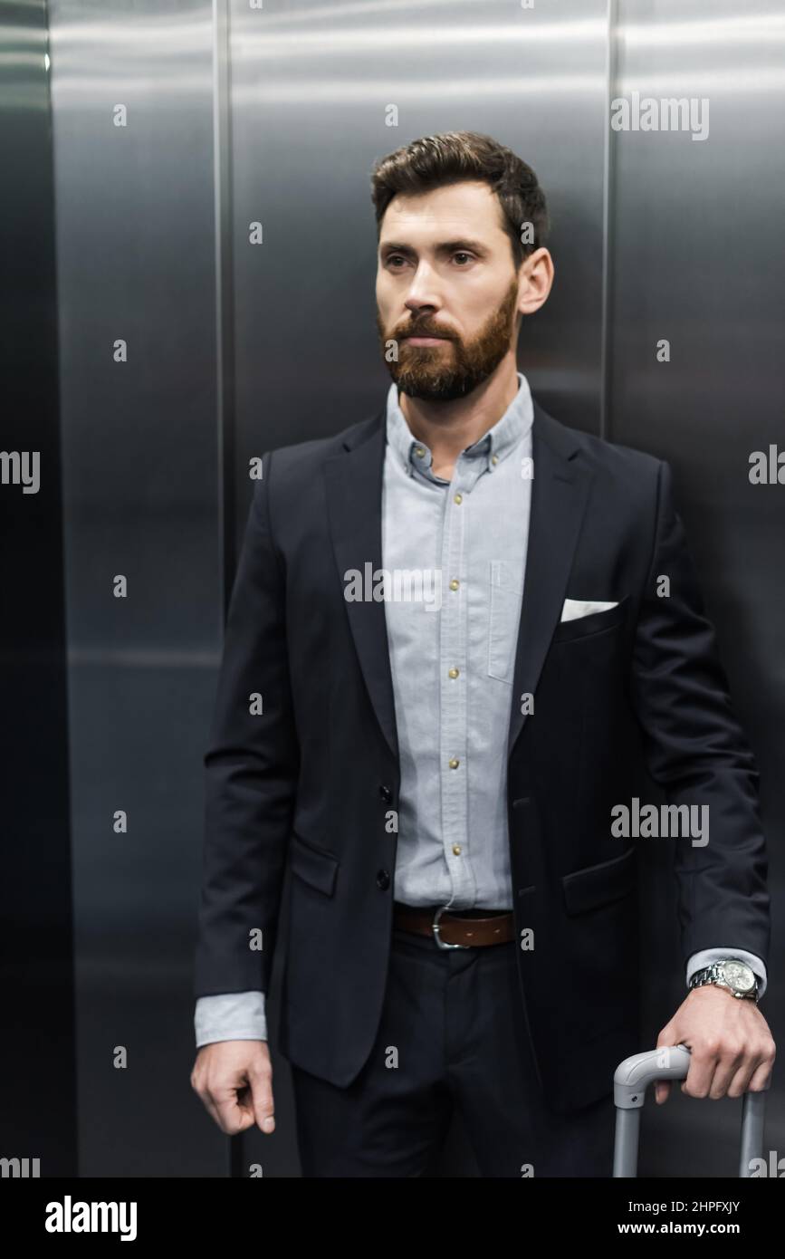 bearded man in suit holding luggage handle in modern elevator Stock ...