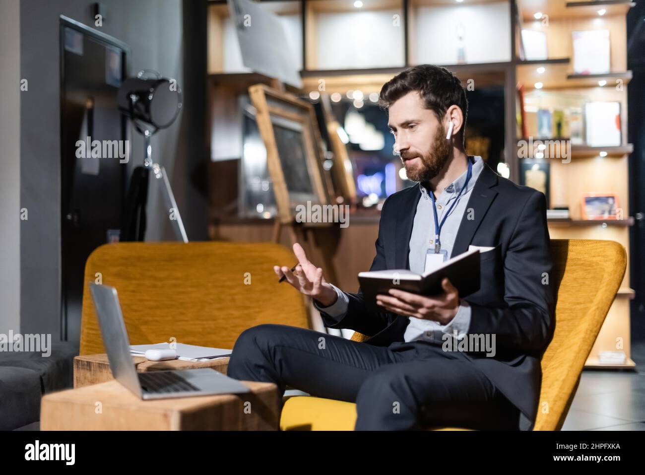 bearded man in earphone having video chat on laptop in hotel foyer ...