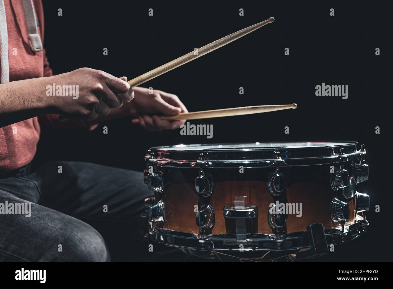 Snare drum and drummer's hands hitting drumsticks against a dark ...