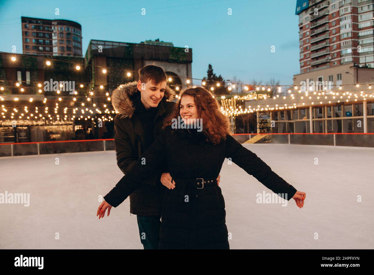 A young couple in love skating on a skating rink, arms apart, look at ...