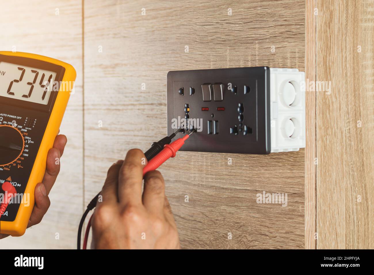 Electrician using a digital meter to measure the voltage at a wall socket on a wooden wall Stock ...
