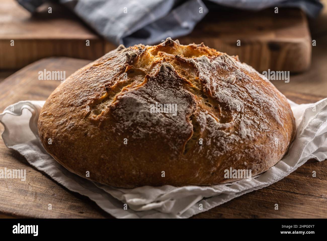 Homemade baked crusty bread places on a linen towel and wooden cutting ...