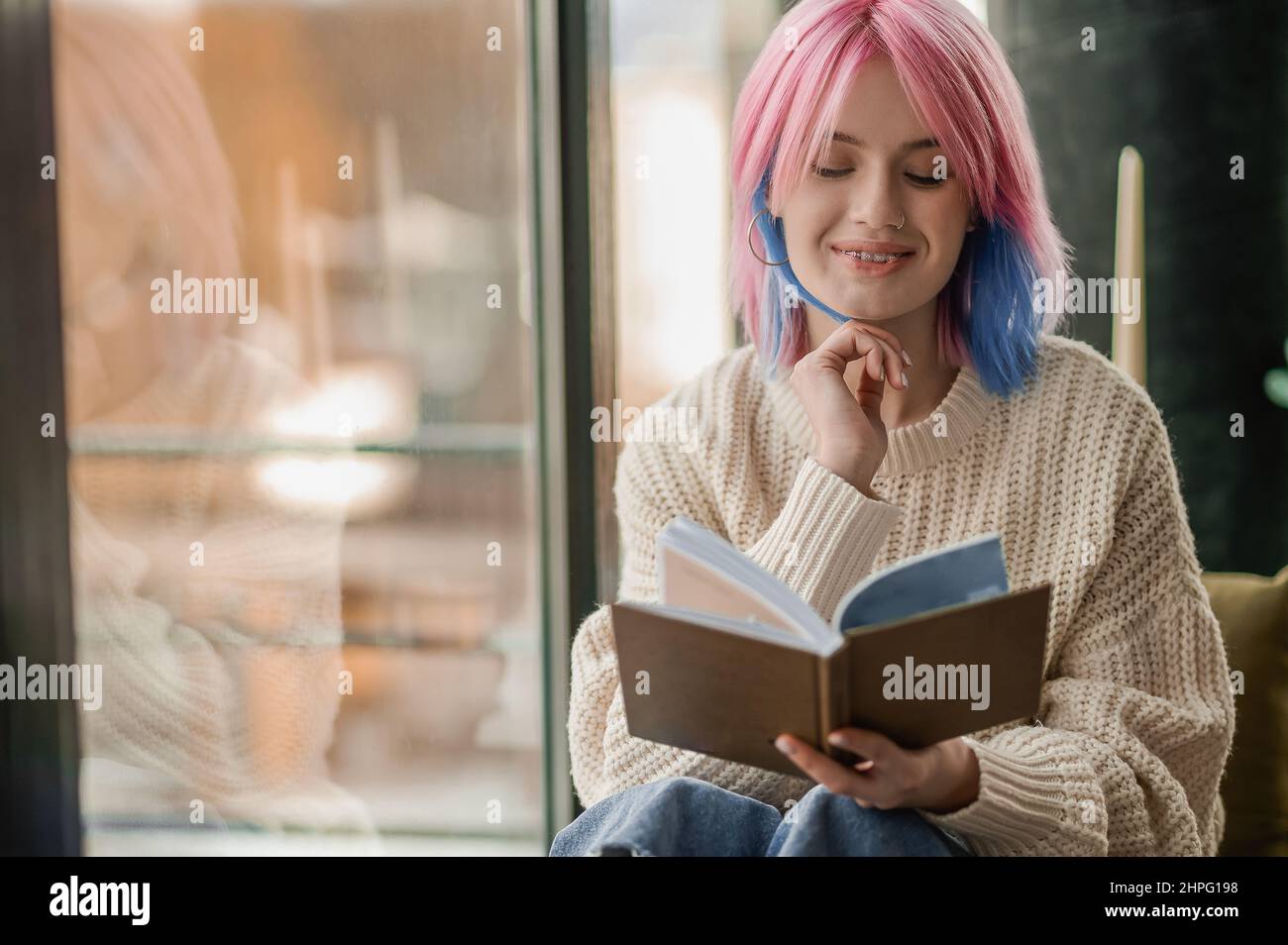 A girl with pink hair reading a book near the window Stock Photo - Alamy