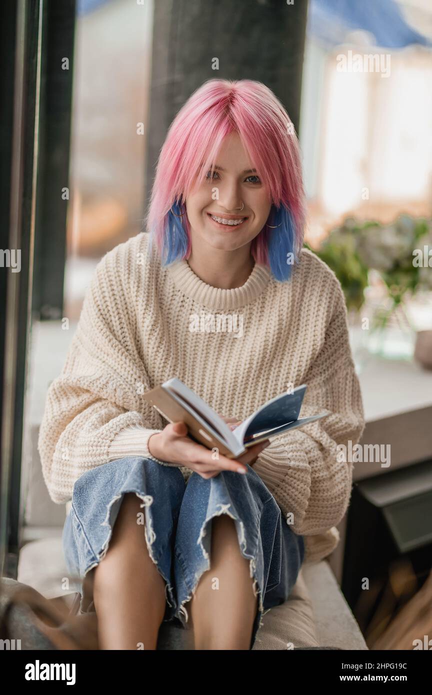 A girl with pink hair reading a book near the window Stock Photo - Alamy