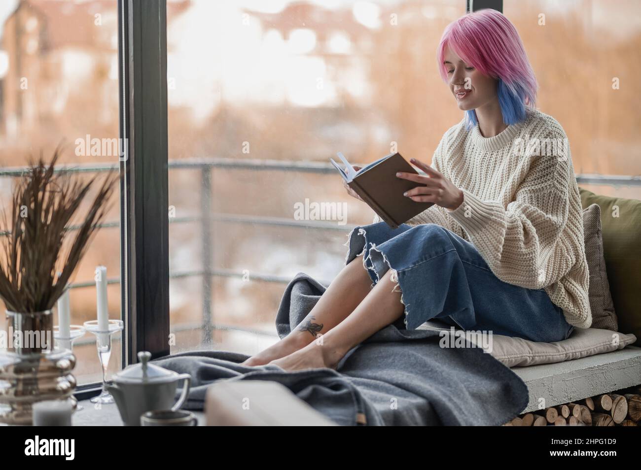 A girl with pink hair reading a book near the window Stock Photo - Alamy