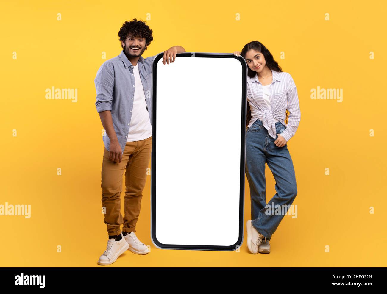 Excited young indian man and woman leaning on giant smartphone with ...