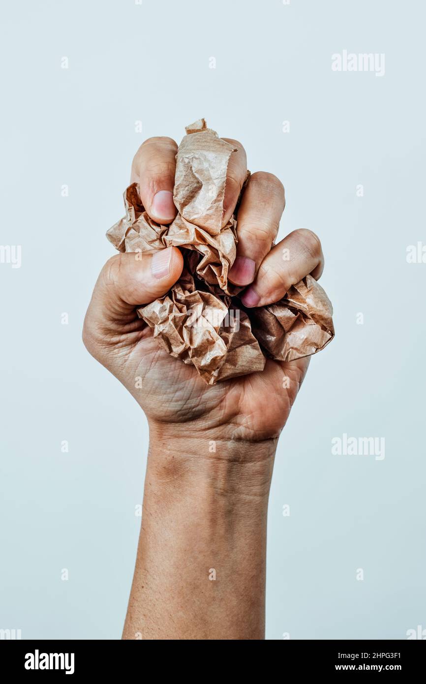 a man squeezes a ball of crumpled brown paper in his hand on an off ...