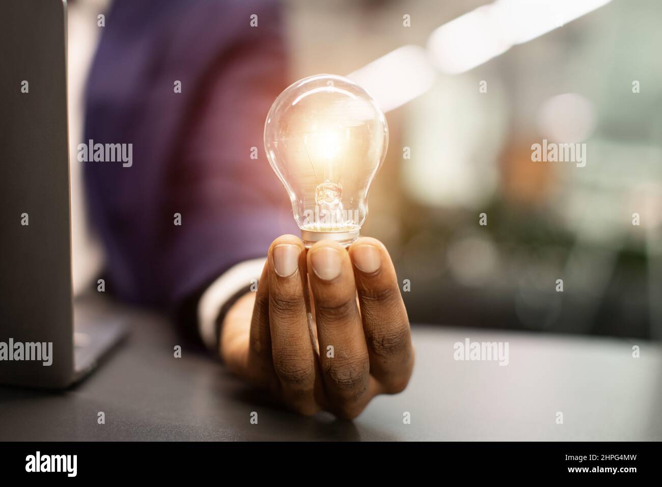 Black businessman holding illuminated light bulb, sitting in office ...