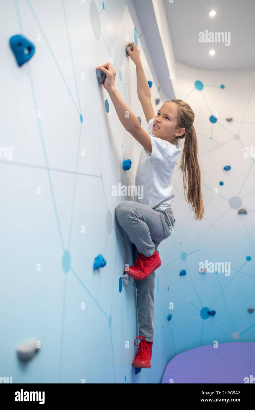 Girl climbing up wall sideways to camera Stock Photo - Alamy