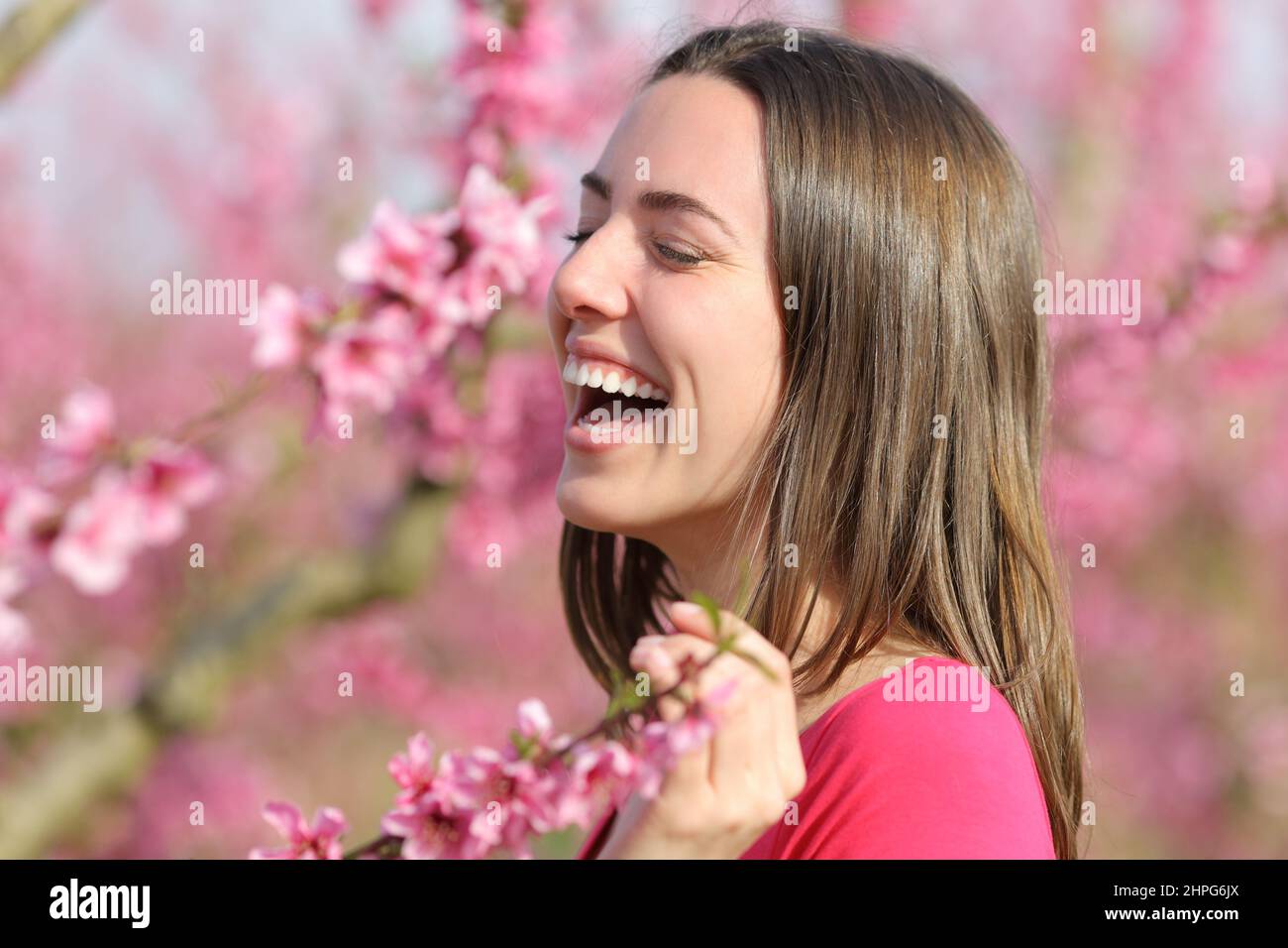 Happy and beautiful woman laughing between pink flowers in a field ...