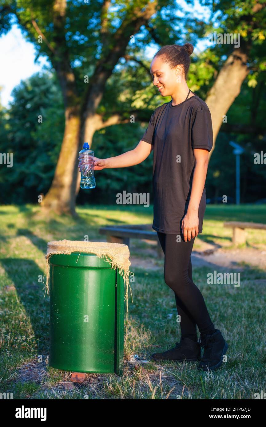 Girl throws trash in the public litter bin in the city park. Preserve ...
