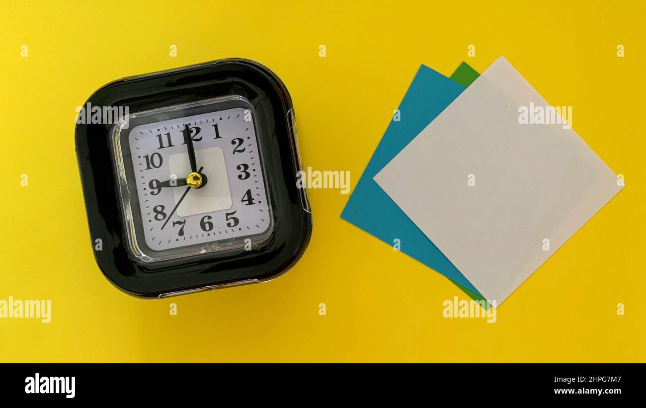 Top view of sticky note and alarm clock with yellow color background ...