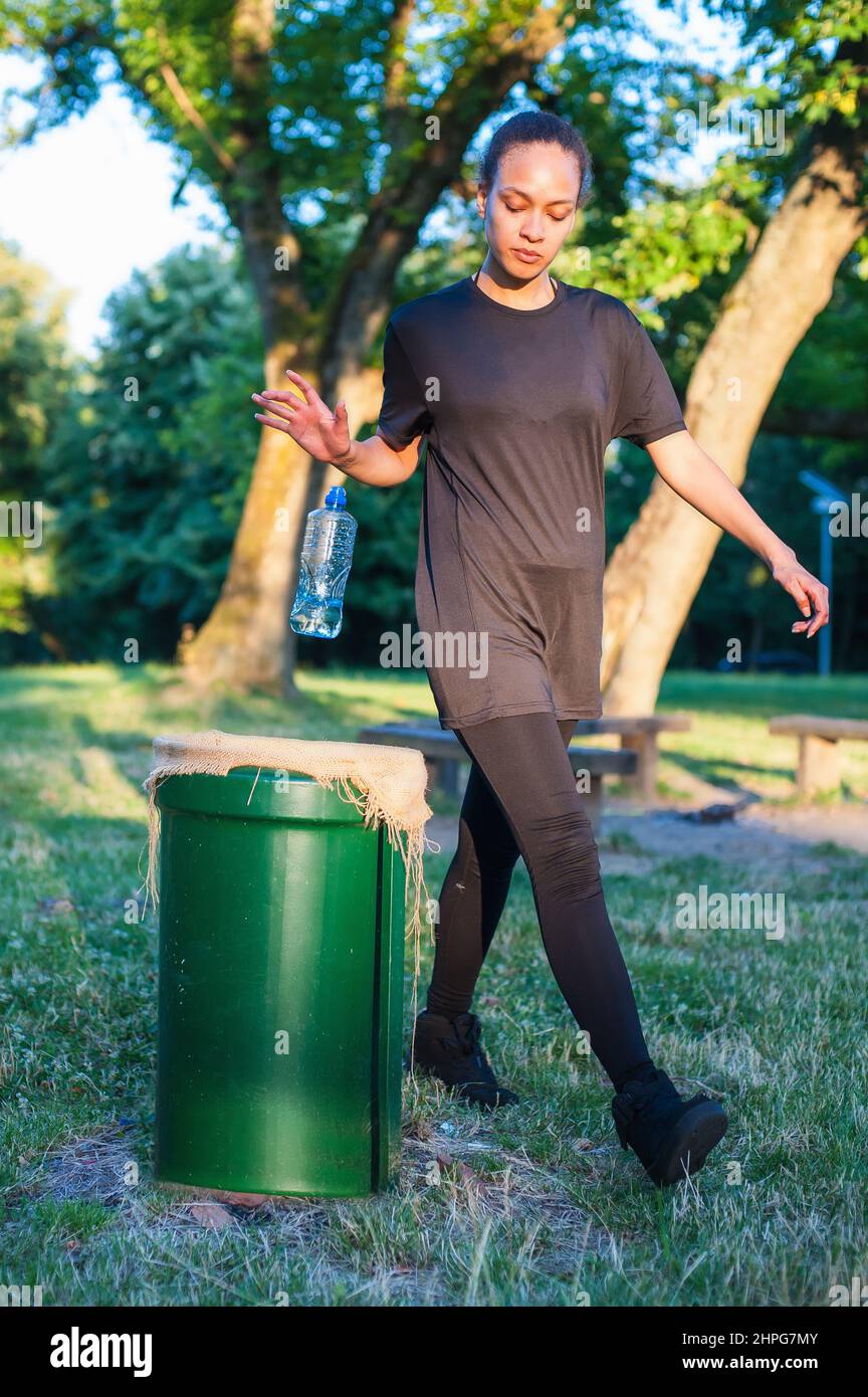 Girl throws trash in the public litter bin in the city park. Preserve ...