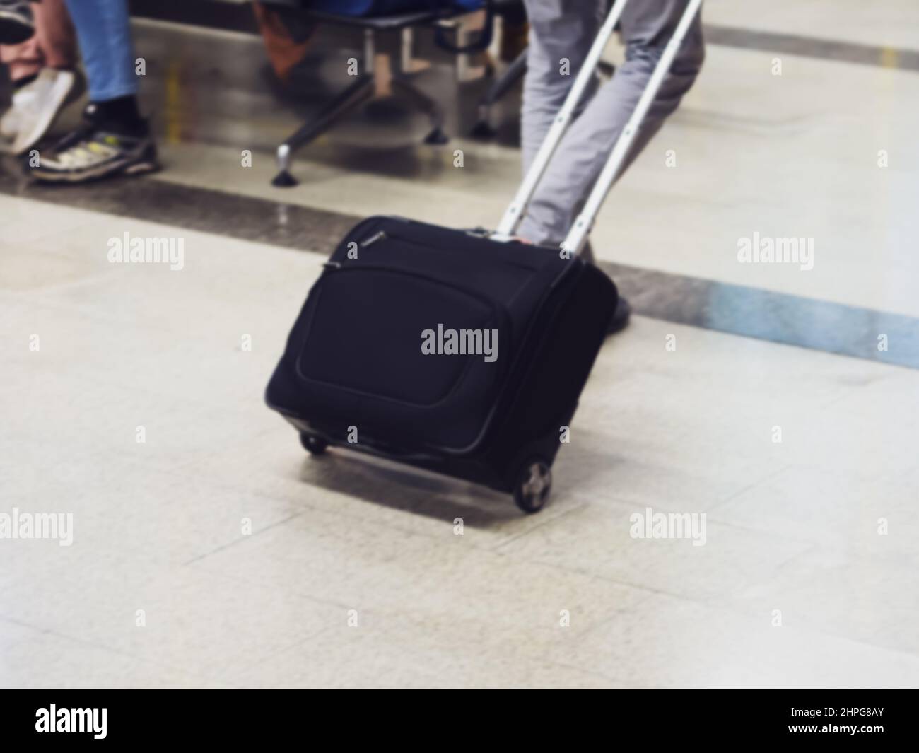 A black bag on wheels is carried by traveler across the marble floor ...