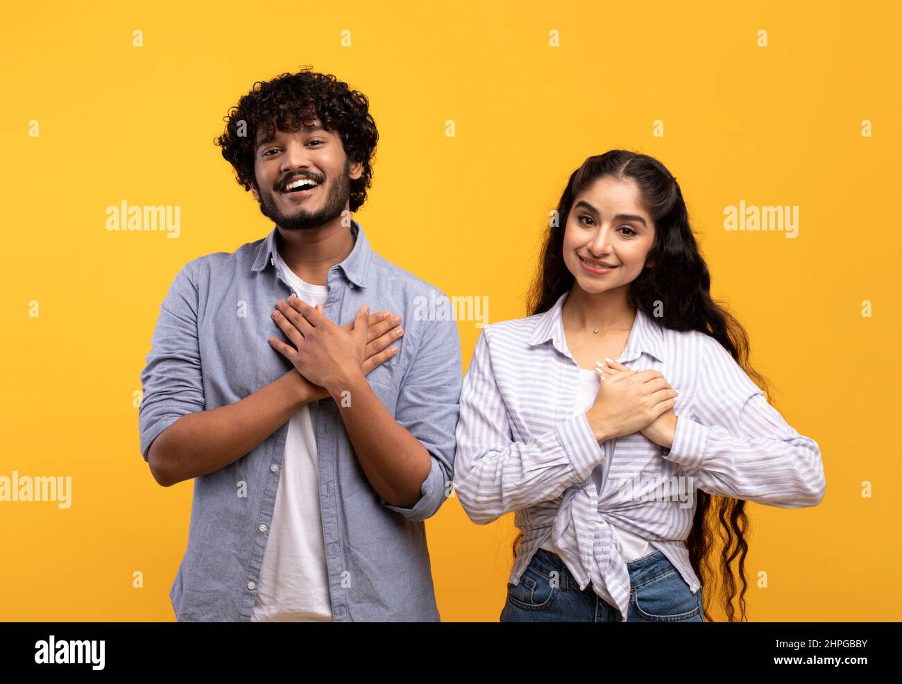Thankful indian couple keeping both palms on chest, smiling at camera ...