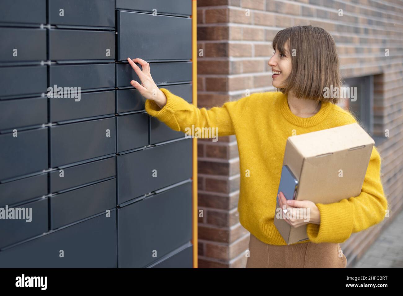 Woman getting parcel from cell of automatic post terminal outdoors ...