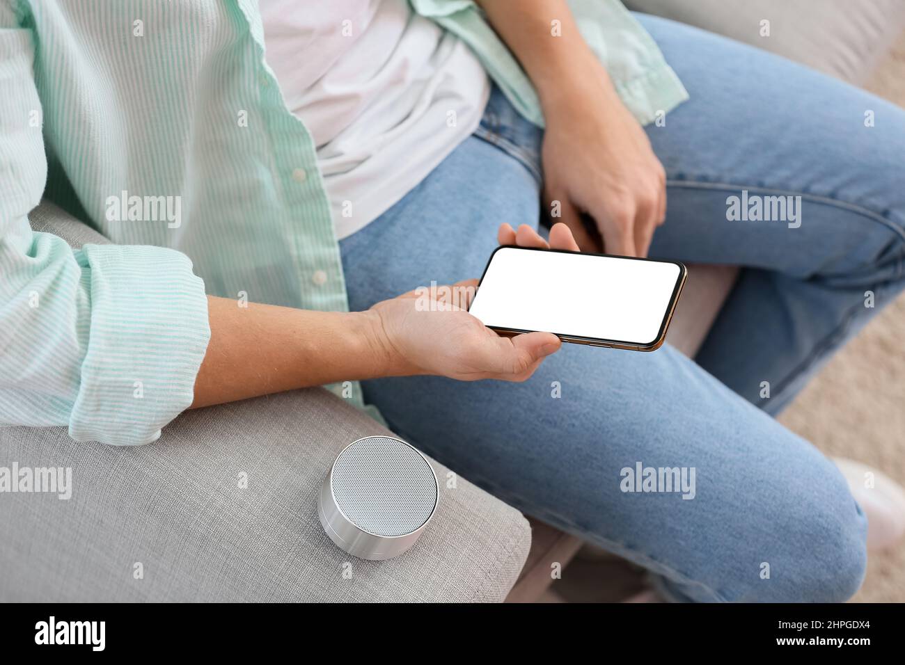 Man connecting mobile phone to wireless portable speaker on sofa ...