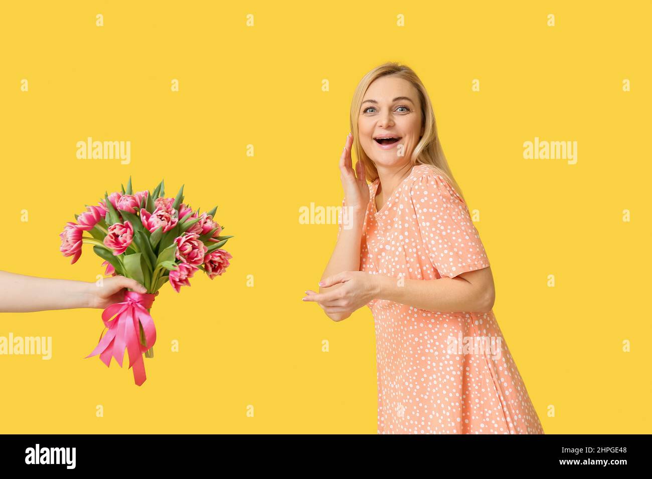 Beautiful woman receiving bouquet of flowers on yellow background ...
