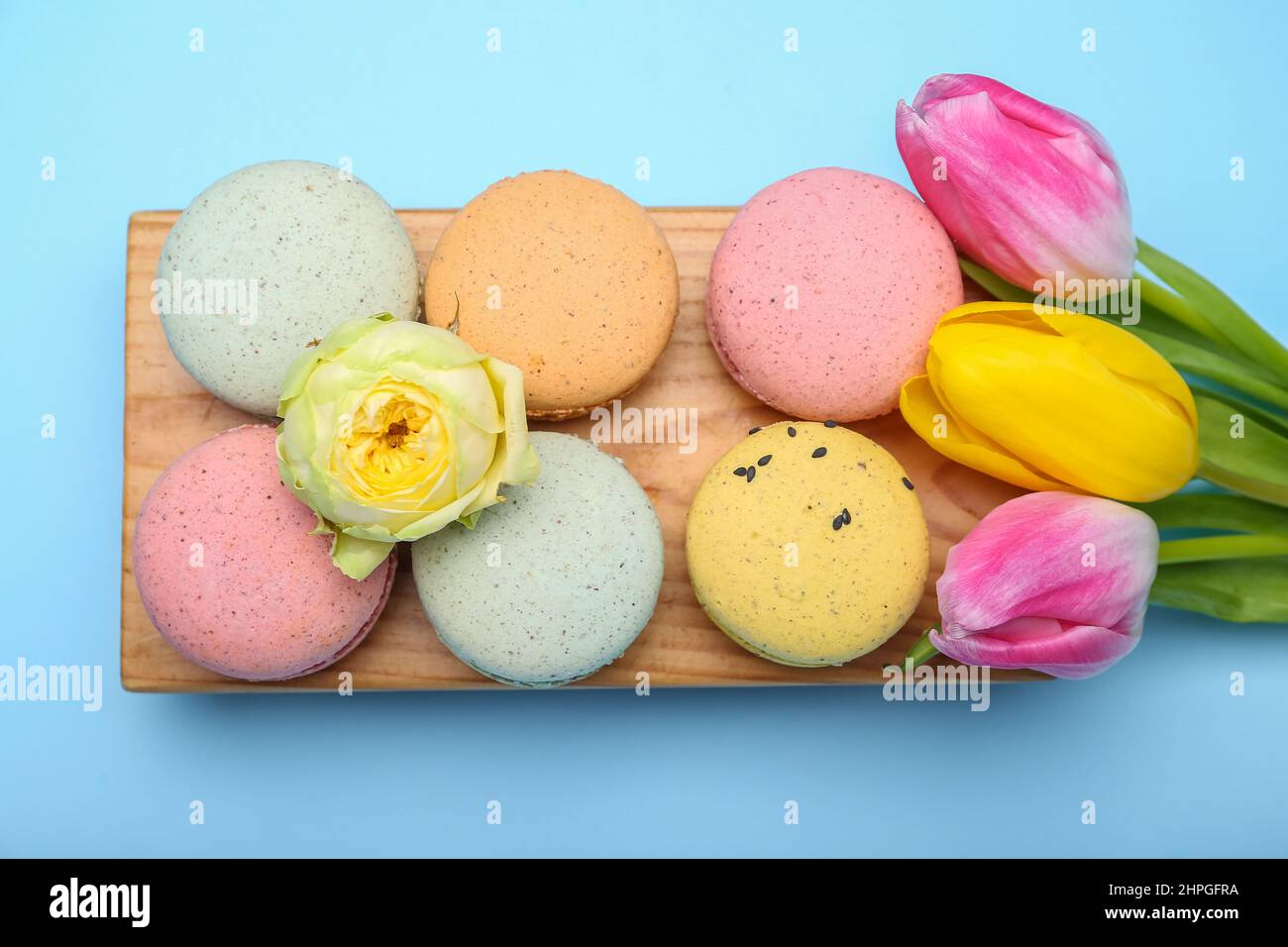 Wooden board with tasty macaroons and flowers on color background ...