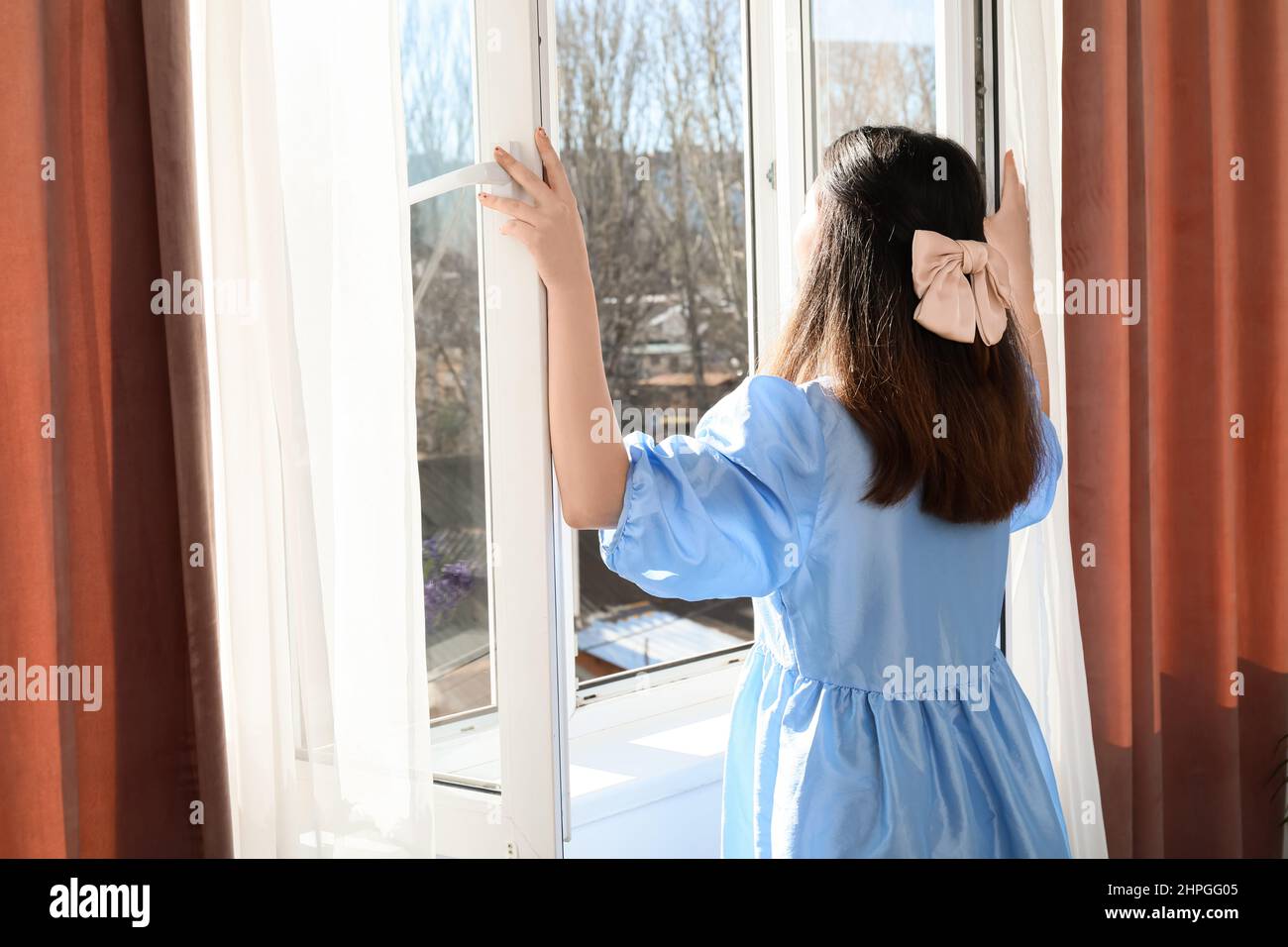 Pretty young Asian woman opening window in room Stock Photo - Alamy
