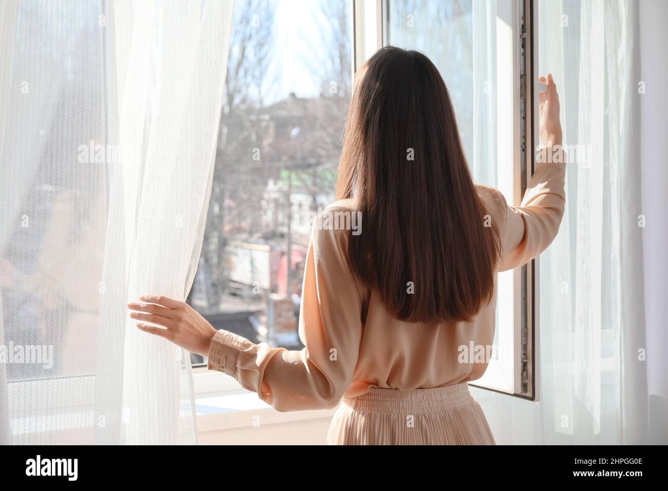 Pretty young woman opening window in room Stock Photo - Alamy