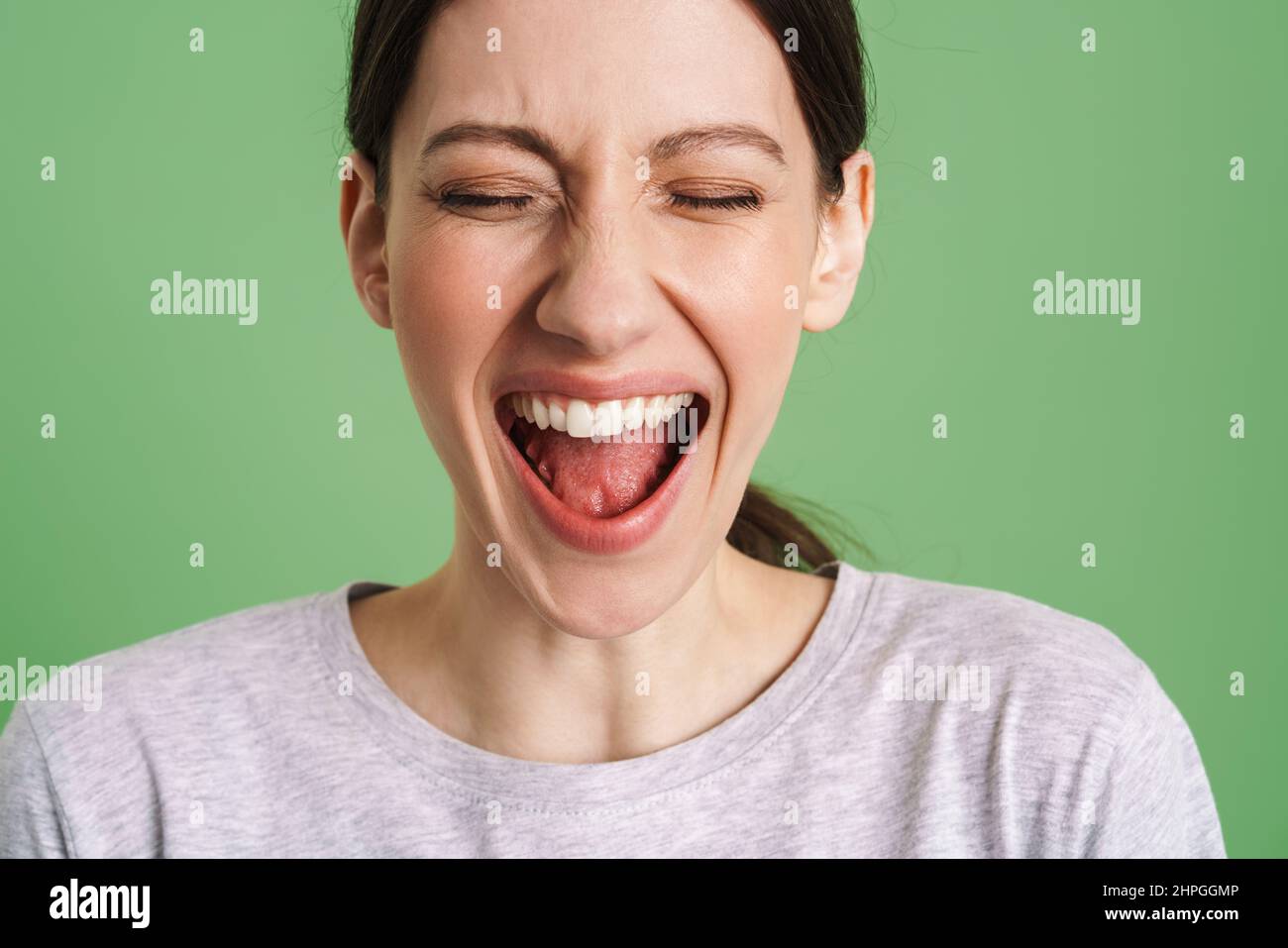 Young brunette woman screaming with her eyes closed isolated over green ...