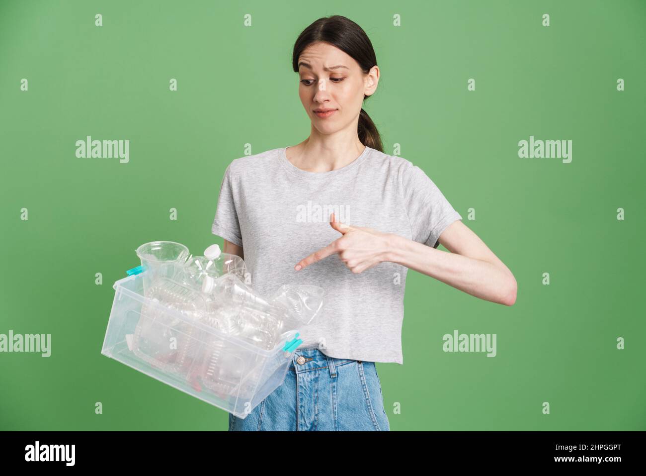 Young brunette woman holding and pointing finger at plastic waste ...