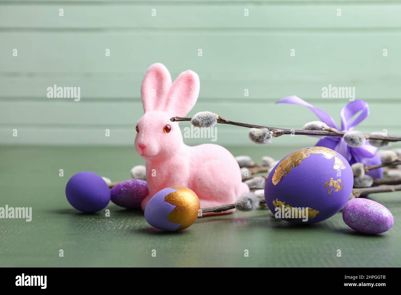 Willow branches, bunny and painted Easter eggs on green wooden ...