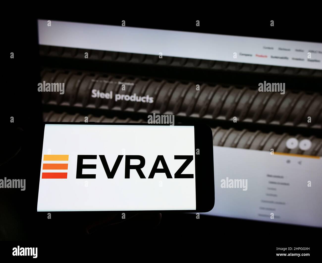 Person holding cellphone with logo of British steel and mining company EVRAZ plc on screen in ...