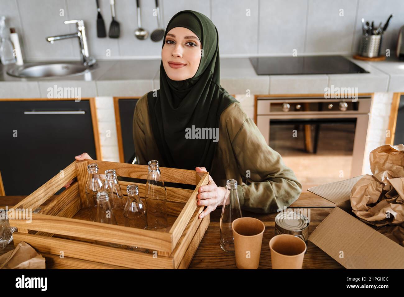 Young muslim woman wearing hijab separating waste while sitting at ...