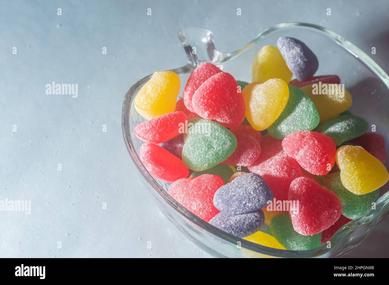 Assorted colorful sweets in a trasparente bowl, light blue background ...