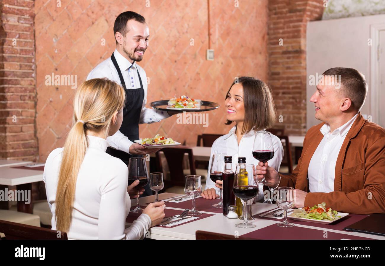 happy waiter placing order in front of guests in country restaurant ...