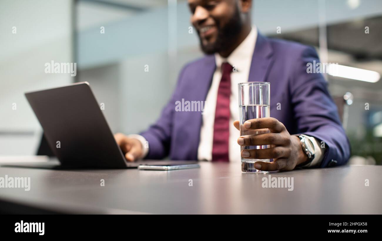 Positive black manager drinking water while working on laptop, panorama ...