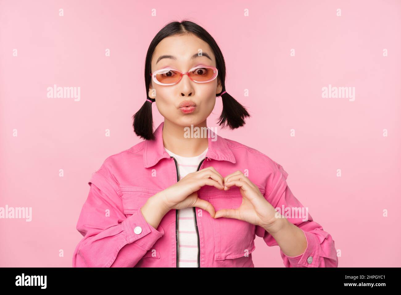 Lovely korean female model in trendy sunglasses, shows heart, care sign ...