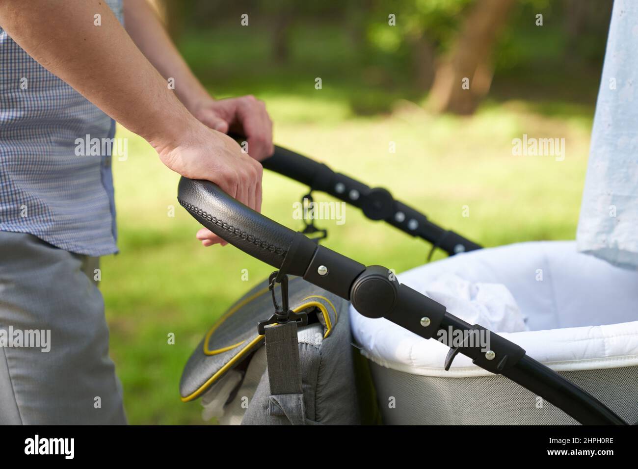 A young dad walking in the park with a baby in a stroller. Close-up of ...