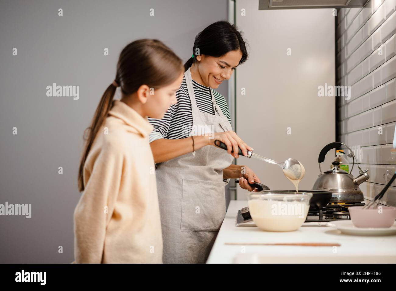Happy beautiful mother and daughter smiling while cooking pancakes in ...