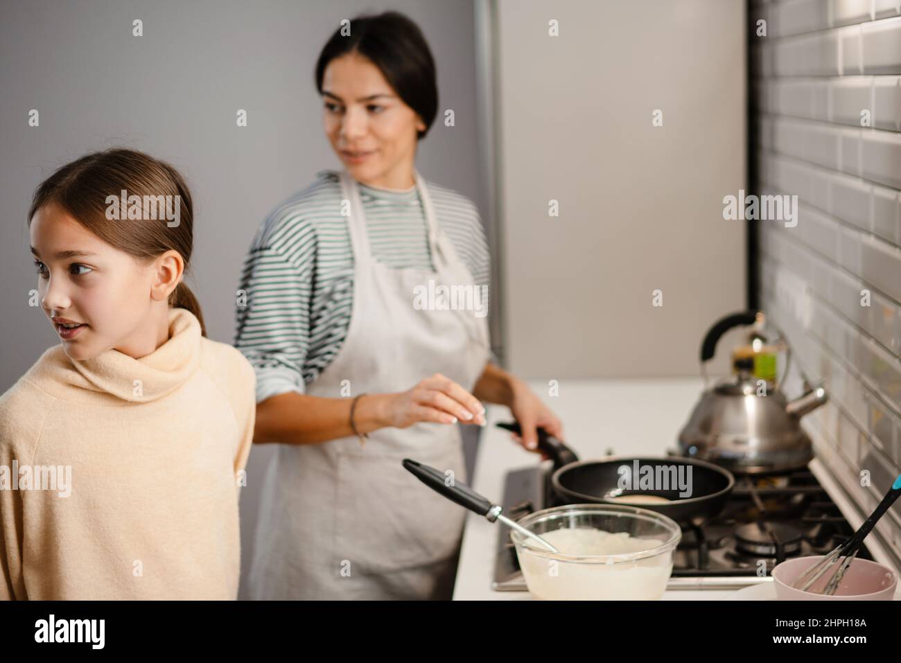 Nice beautiful mother and daughter cooking pancakes in cozy kitchen ...
