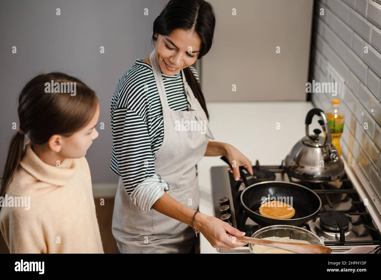 Happy beautiful mother and daughter smiling while cooking pancakes in ...