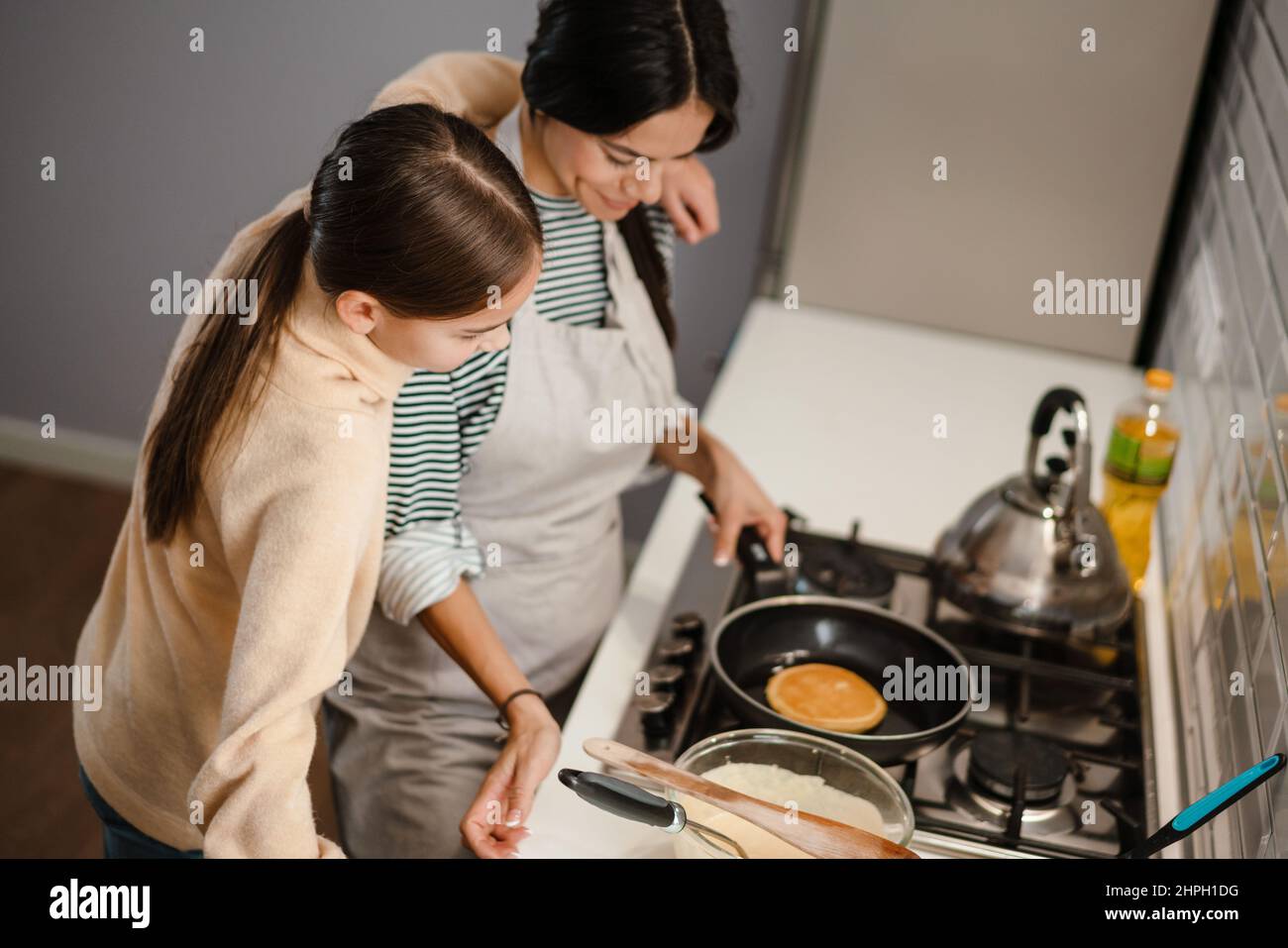 Happy beautiful mother and daughter smiling while cooking pancakes in ...