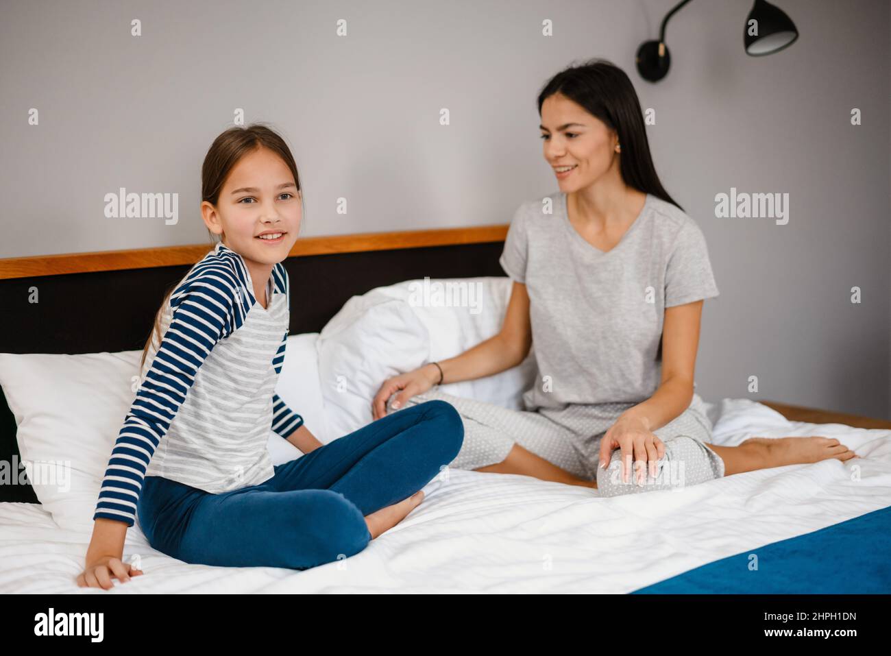Joyful beautiful mother and daughter talking while sitting on bed at home Stock Photo - Alamy