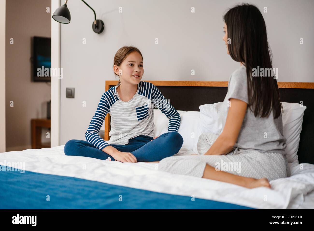 Happy beautiful mother and daughter talking while sitting on bed at home Stock Photo - Alamy