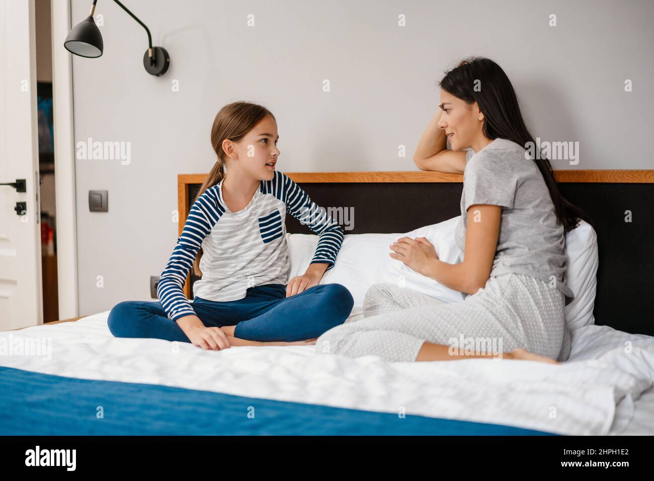 Happy beautiful mother and daughter talking while sitting on bed at home Stock Photo - Alamy