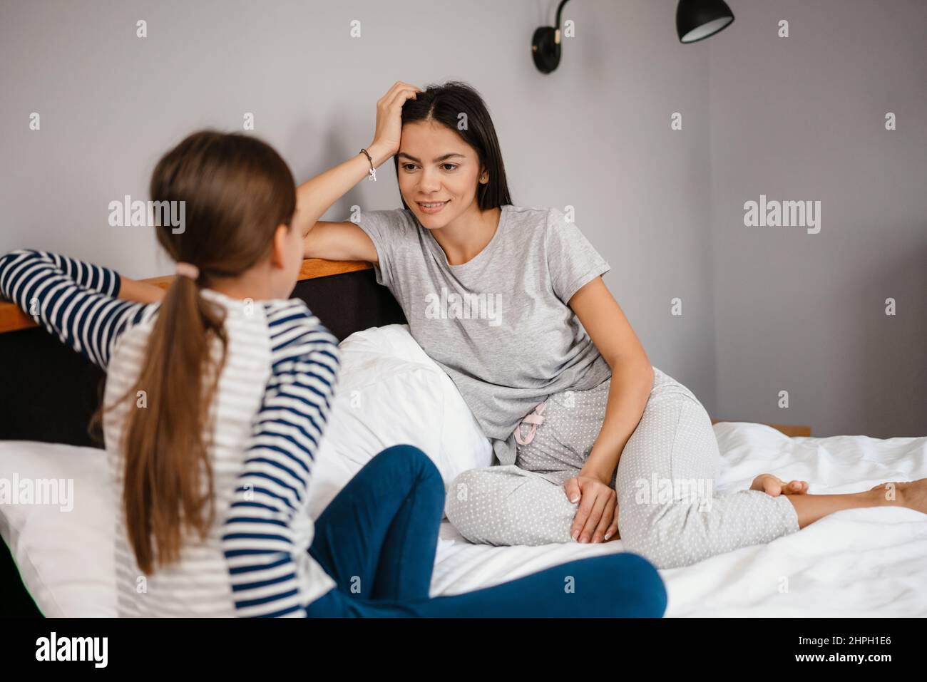 Happy beautiful mother and daughter talking while sitting on bed at home Stock Photo - Alamy
