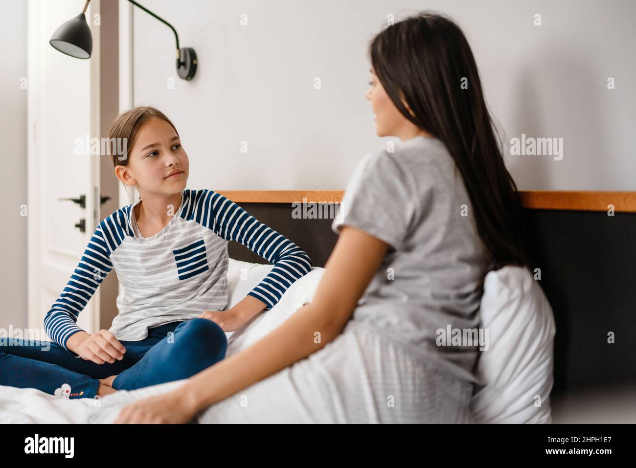 Happy beautiful mother and daughter talking while sitting on bed at home Stock Photo - Alamy