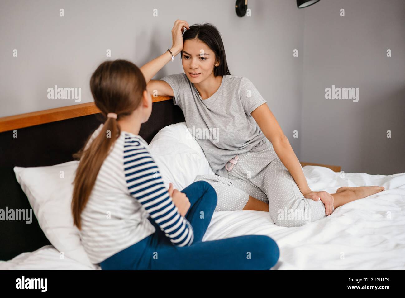 Happy beautiful mother and daughter talking while sitting on bed at home Stock Photo - Alamy
